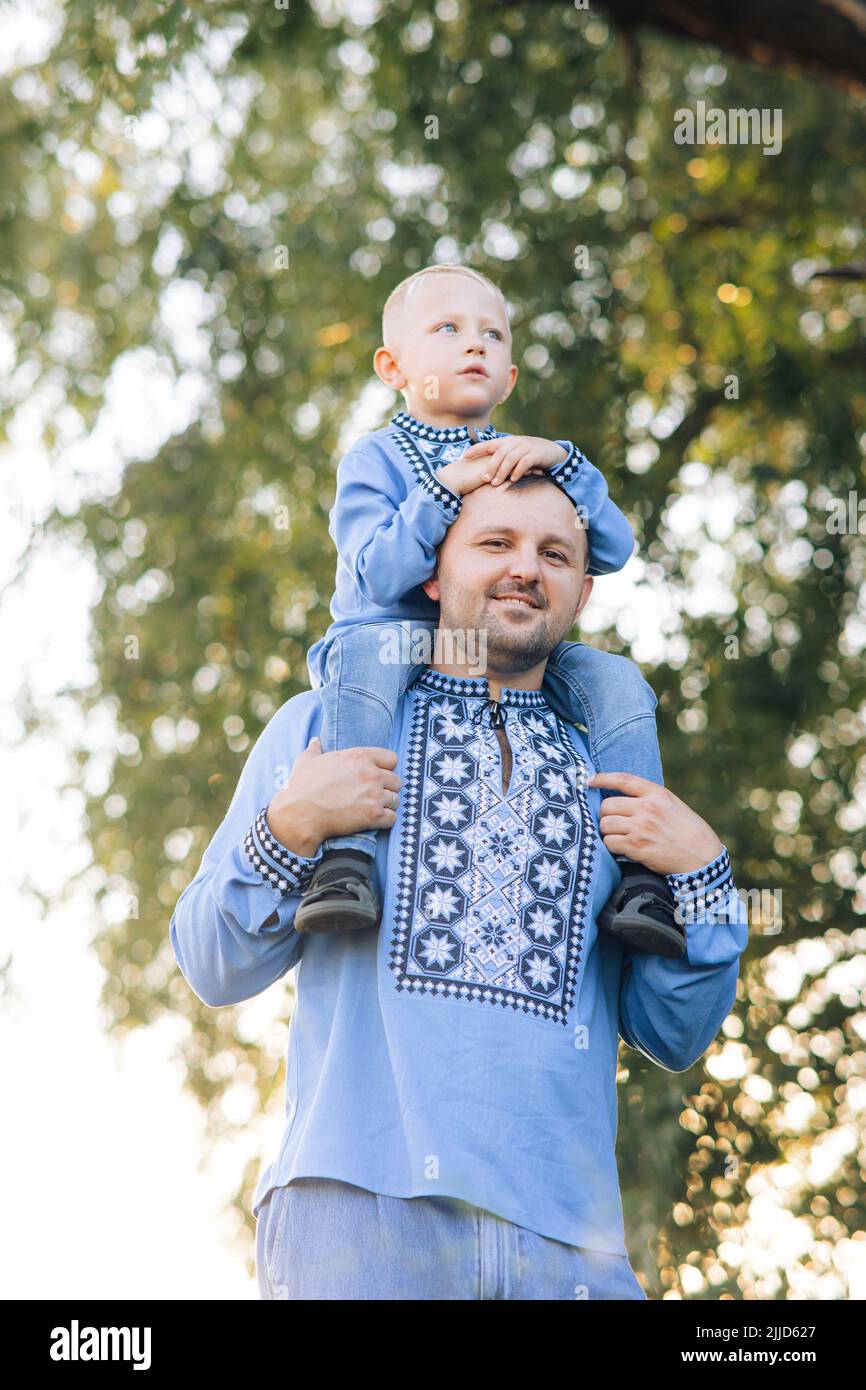 Happy father carries his son on his shoulders during walk on park. They ...