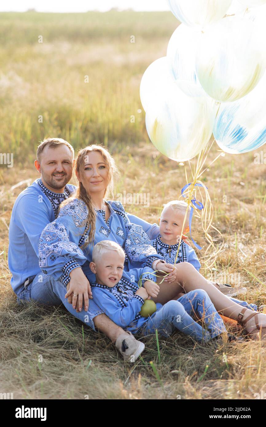 Happy parents with two their twins sons sit on grass and rest on meadow ...