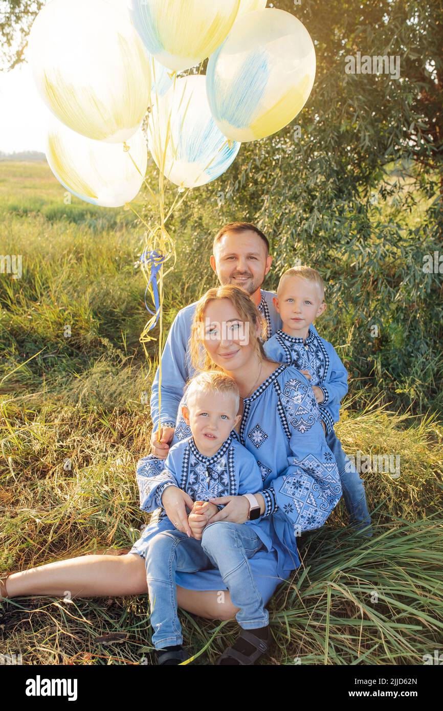 Happy parents with two their twins sons sit on grass and rest on meadow ...