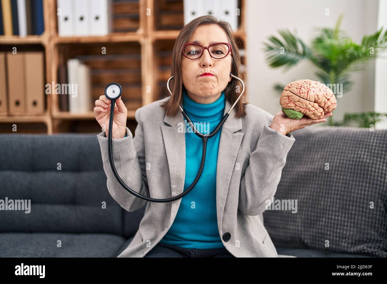 Middle age hispanic woman working at therapy office holding brain ...