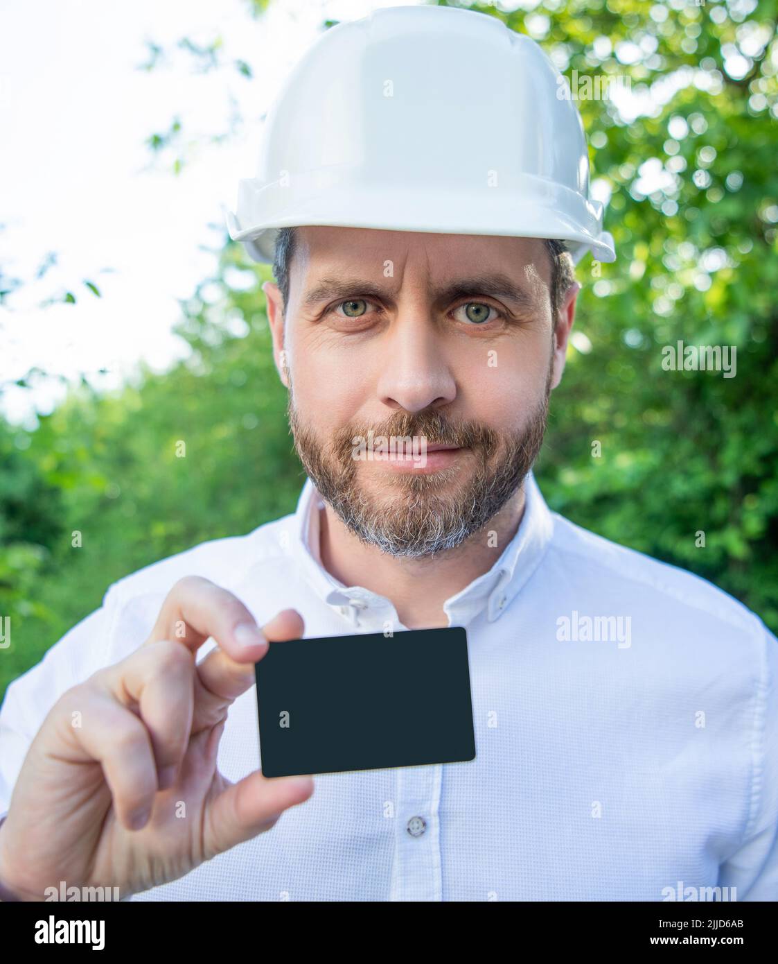 Man architect in hardhat showing blank contact card outdoors, copy ...