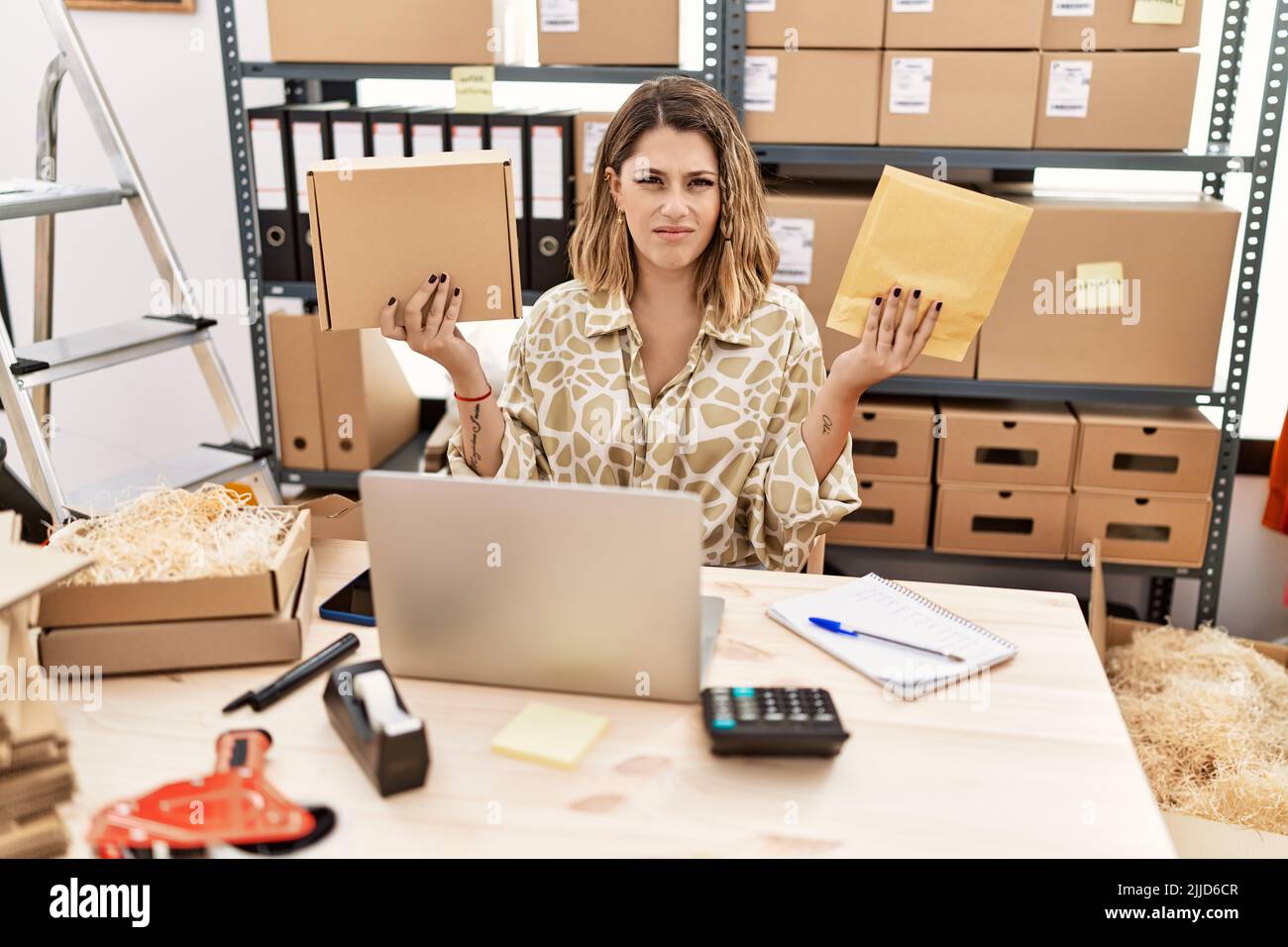 Young hispanic woman holding package and envelope sitting on desk ...