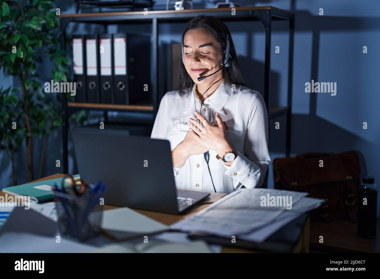 Young brunette woman wearing call center agent headset working late at ...
