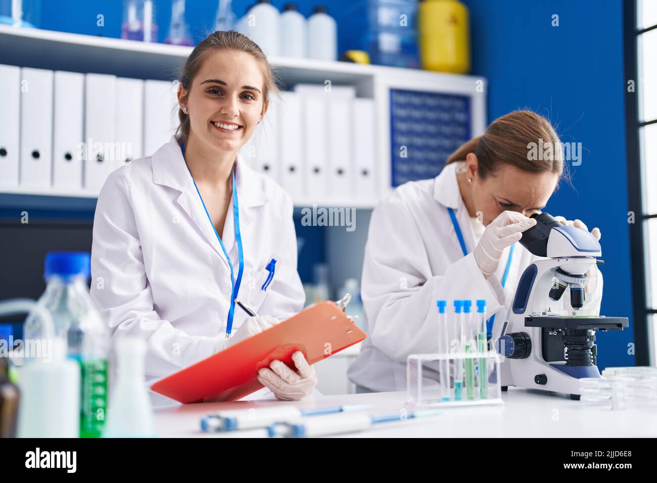 Two women scientists using microscope and write on document at ...