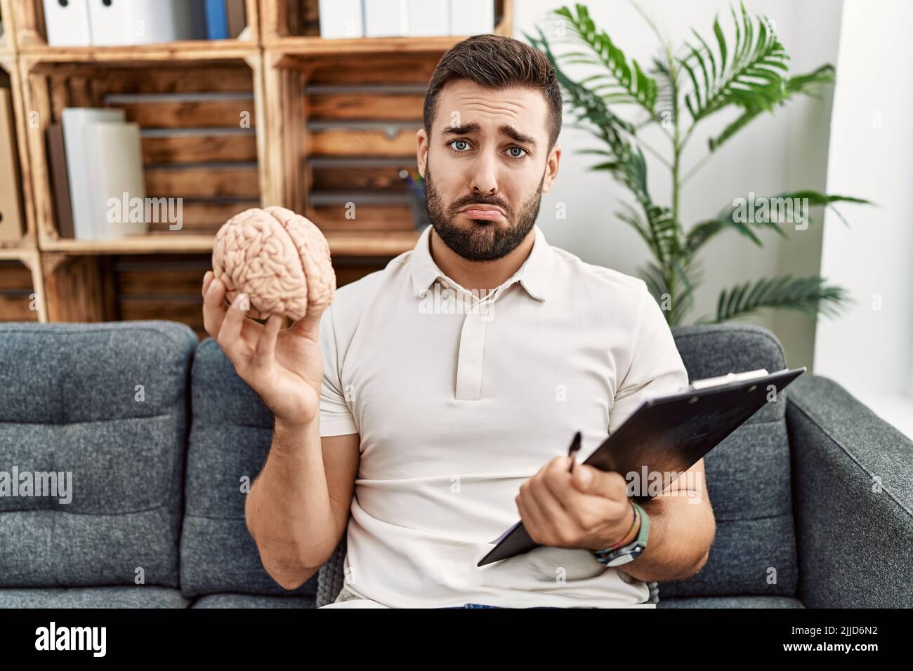 Handsome hispanic man holding brain working at psychology clinic ...