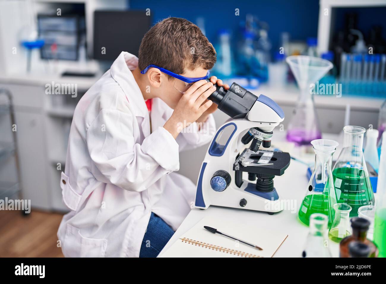 Blond child wearing scientist uniform using microscope at laboratory ...