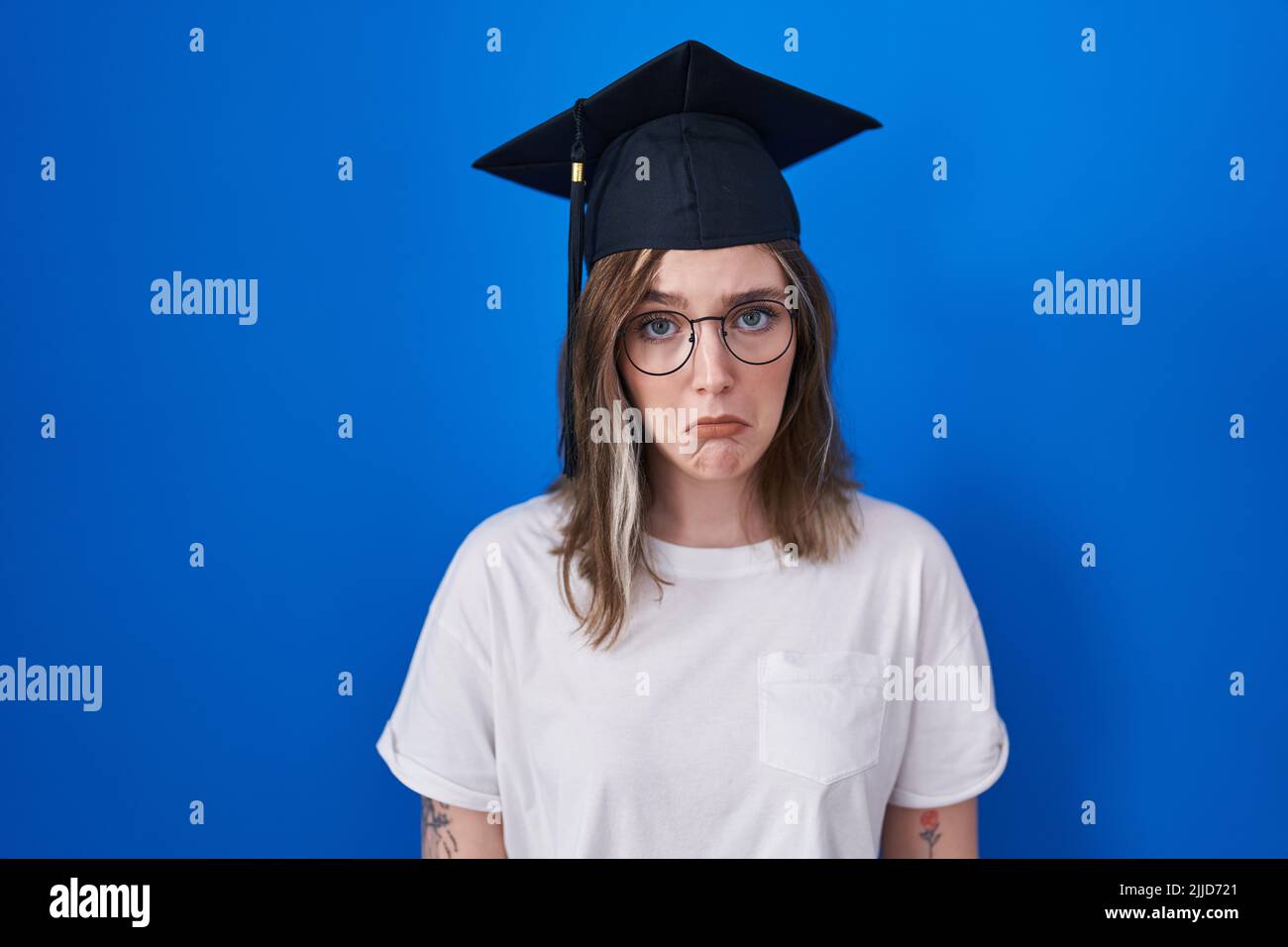 Blonde caucasian woman wearing graduation cap depressed and worry for ...