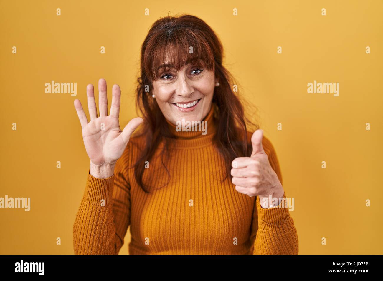 Middle age hispanic woman standing over yellow background showing and ...