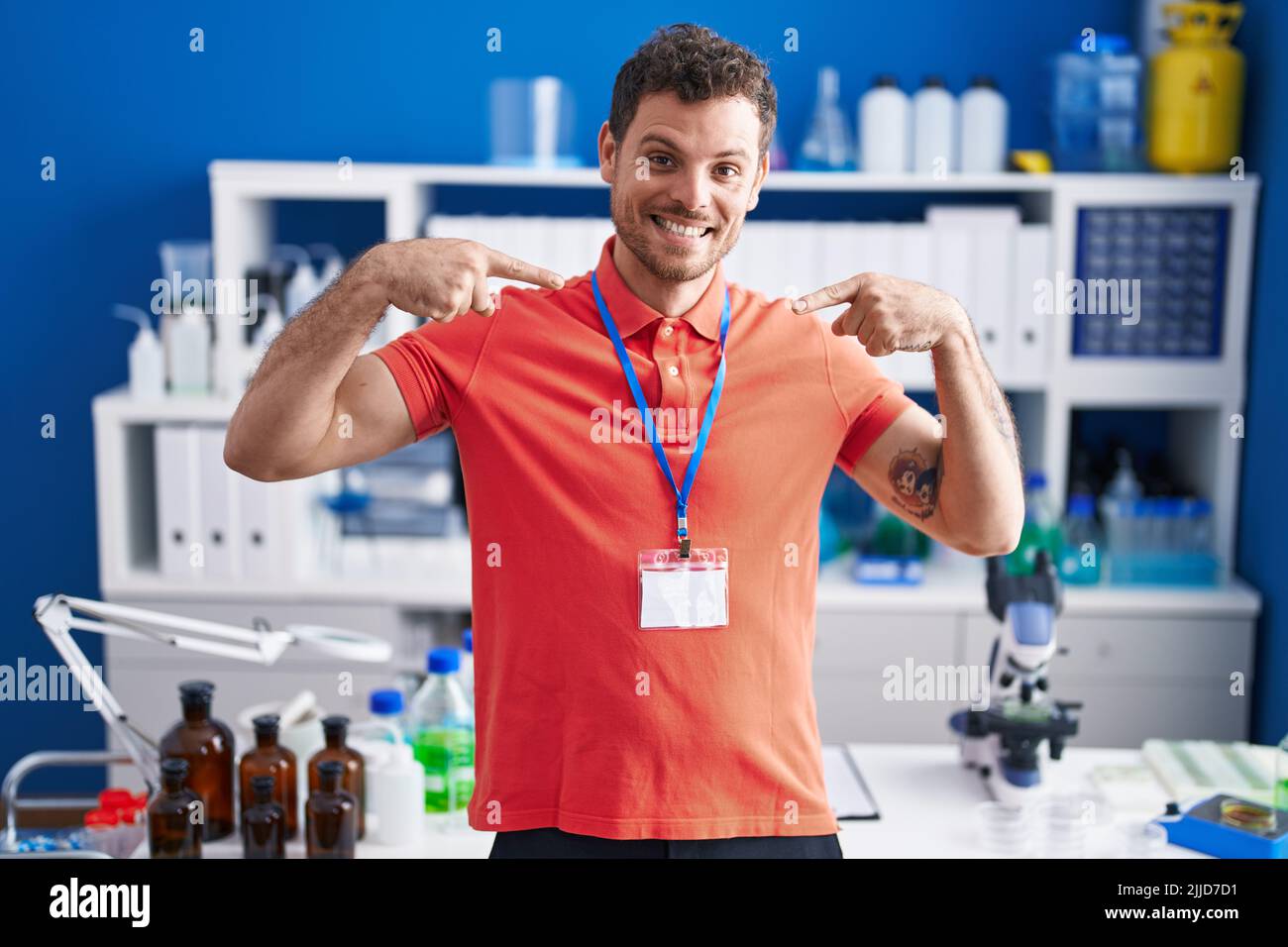 Young hispanic man working at scientist laboratory looking confident with smile on face ...