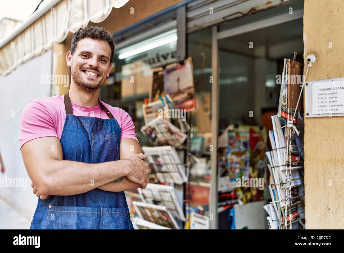 Young hispanic worker wearing apron standing with arms crossed gesture ...