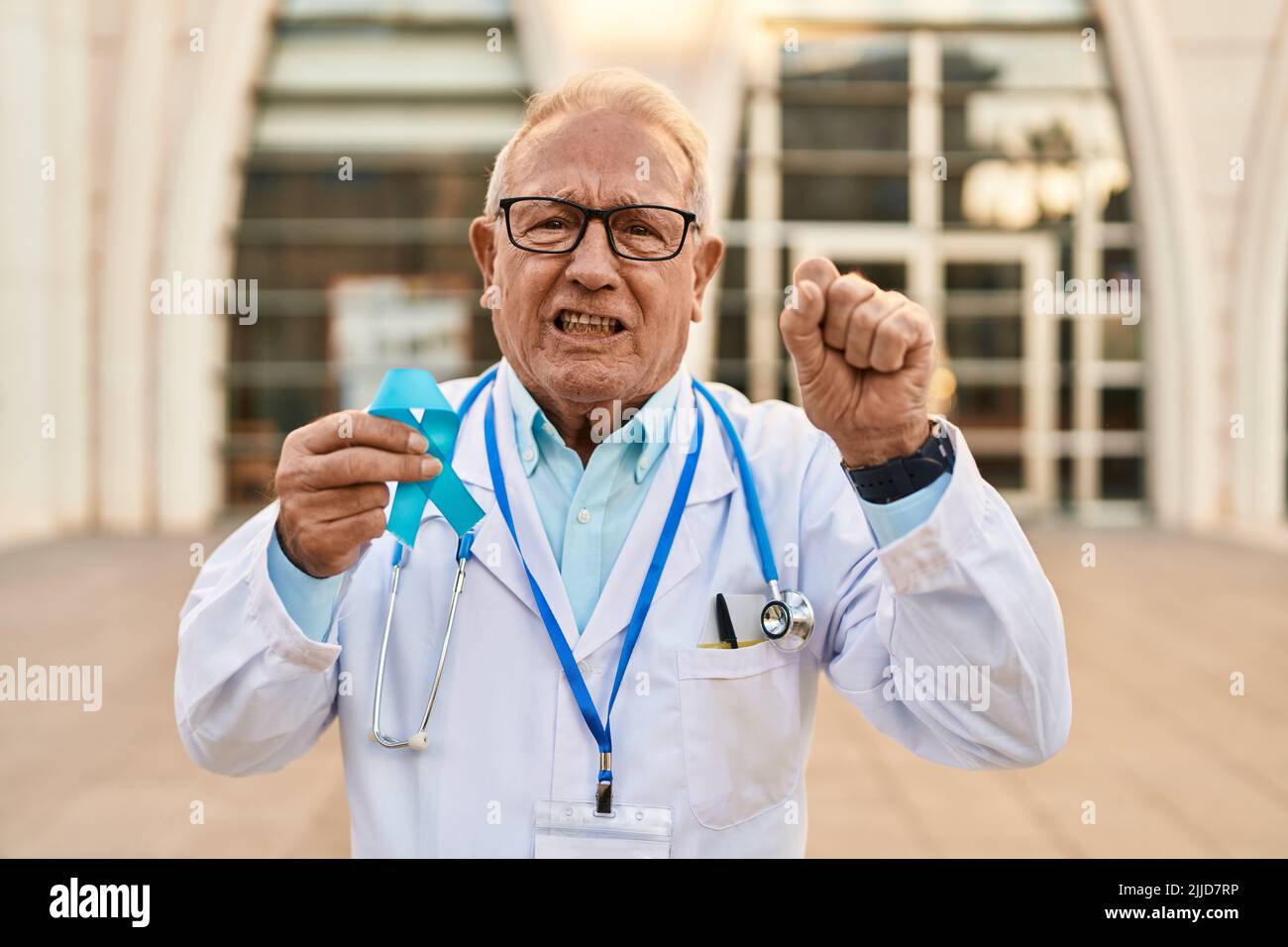 Senior doctor with grey hair holding blue ribbon annoyed and frustrated ...