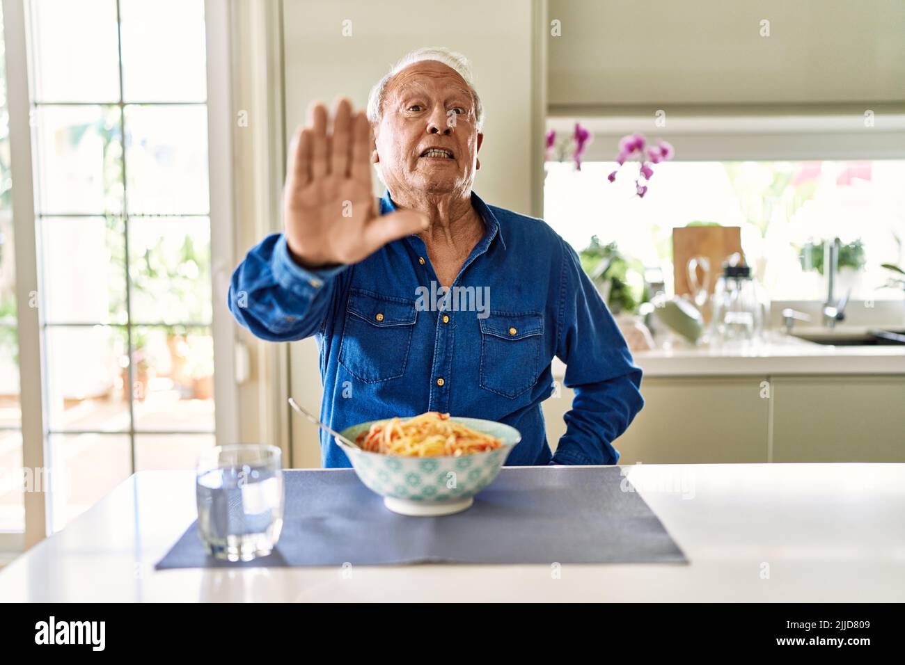 Senior man with grey hair eating pasta spaghetti at home doing stop ...