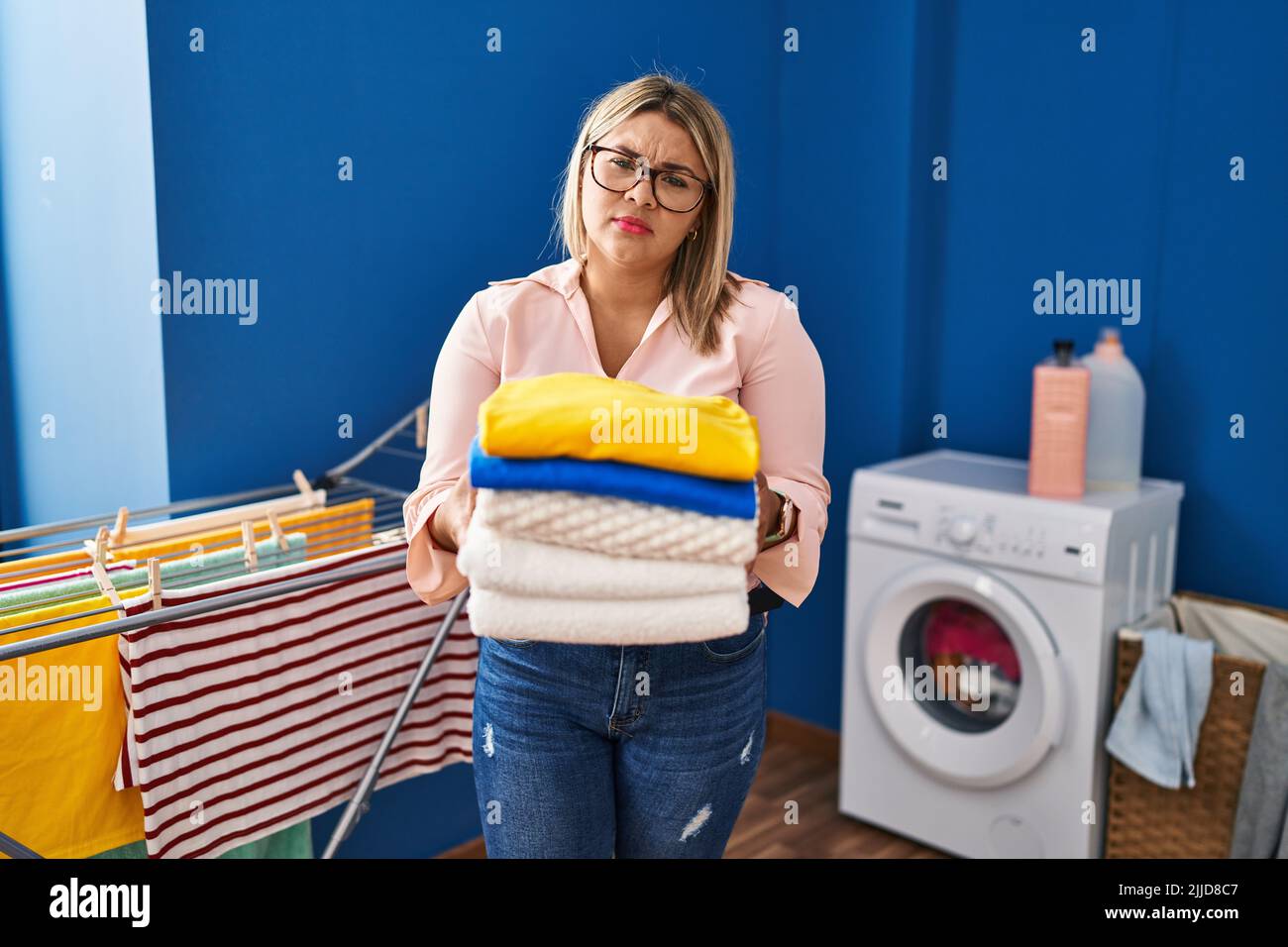 Young hispanic woman holding folded laundry after ironing depressed and worry for distress ...