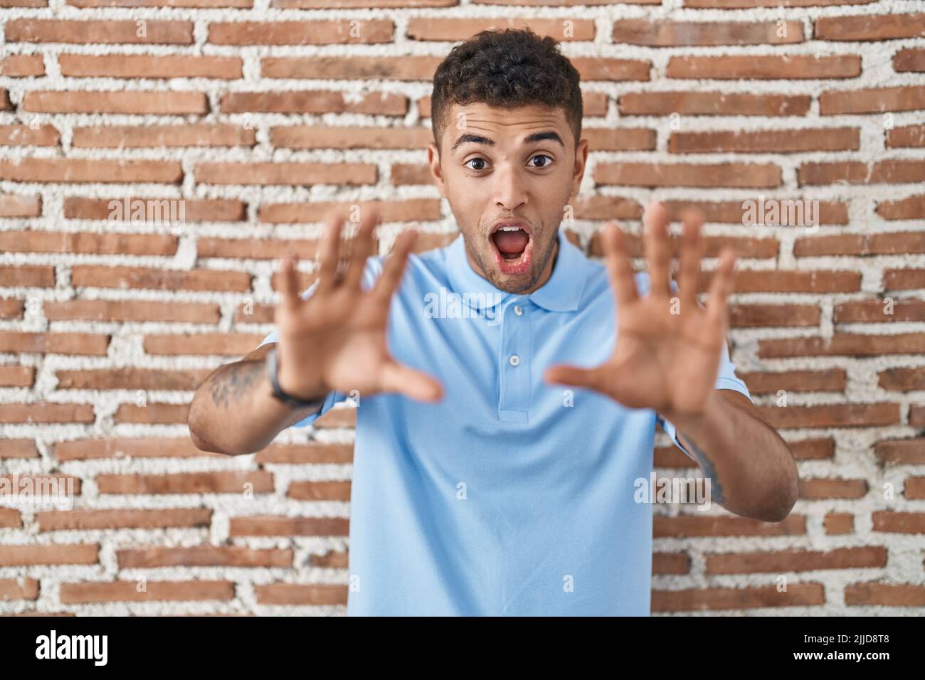 Brazilian young man standing over brick wall doing stop gesture with ...