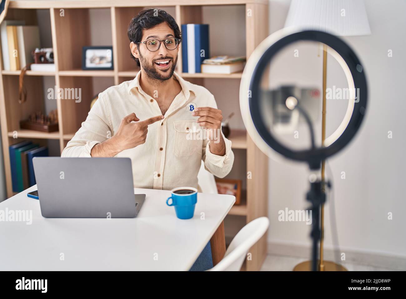 Handsome latin man recording bitcoin tutorial with smartphone at home ...