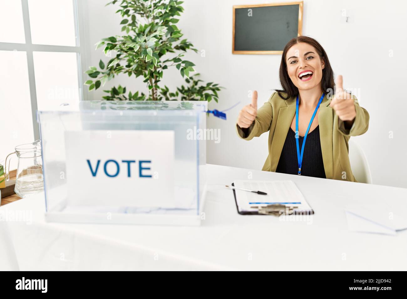 Young brunette woman sitting at election table with voting ballot ...
