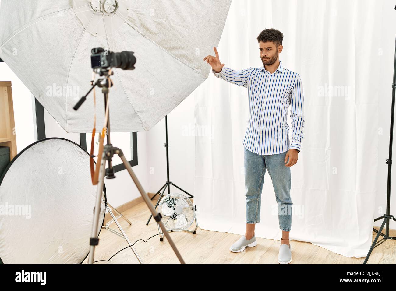 Arab young man posing as model at photography studio pointing with finger up and angry ...