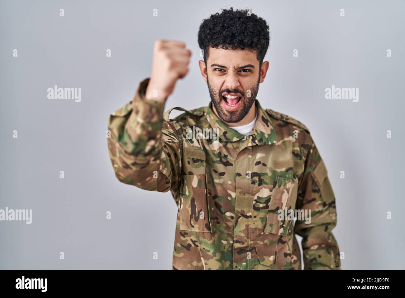 Arab man wearing camouflage army uniform angry and mad raising fist ...