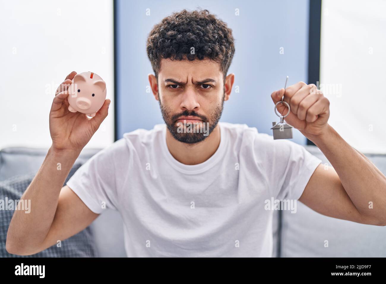 Arab man holding piggy bank and house keys depressed and worry for ...
