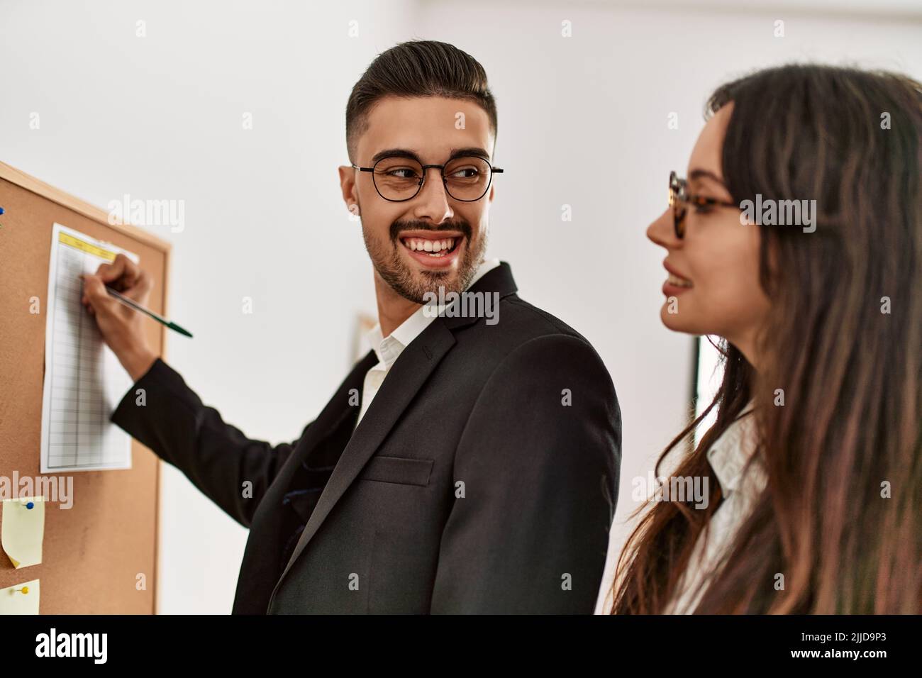 Two business workers smiling happy writing on corkboard reminder at the ...