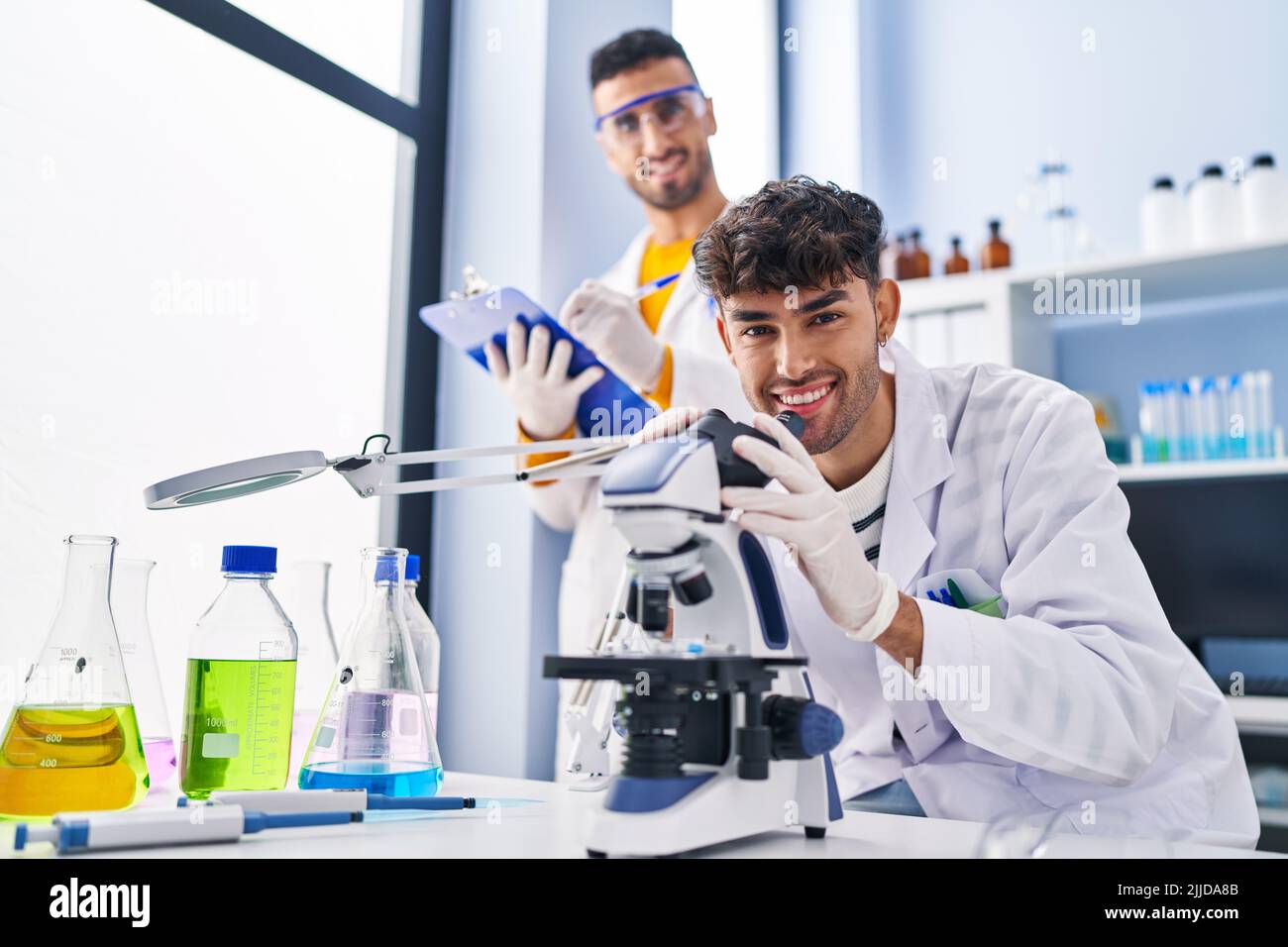 Two man scientists using microscope write on clipboard working at ...