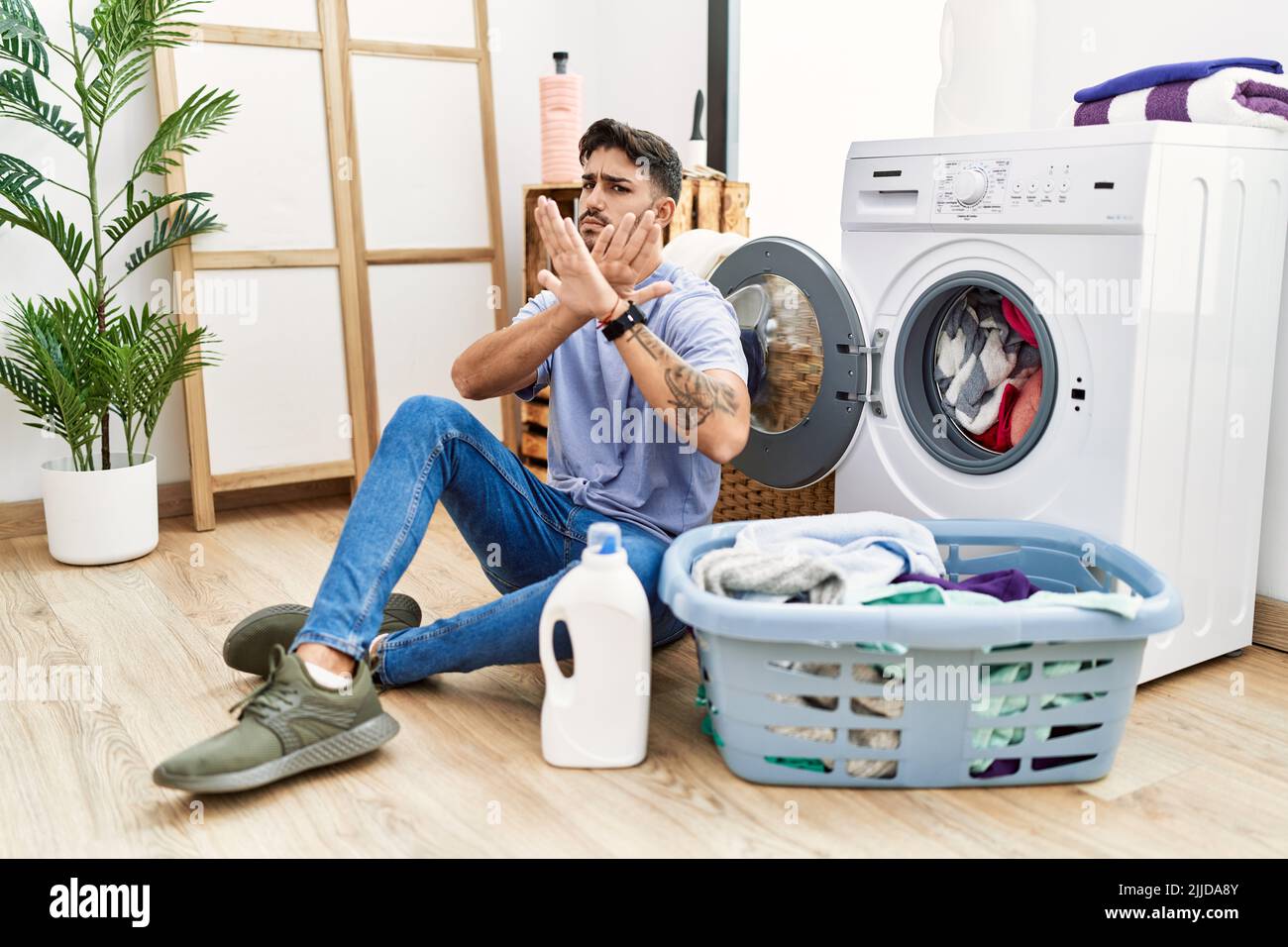 Young hispanic man putting dirty laundry into washing machine rejection ...