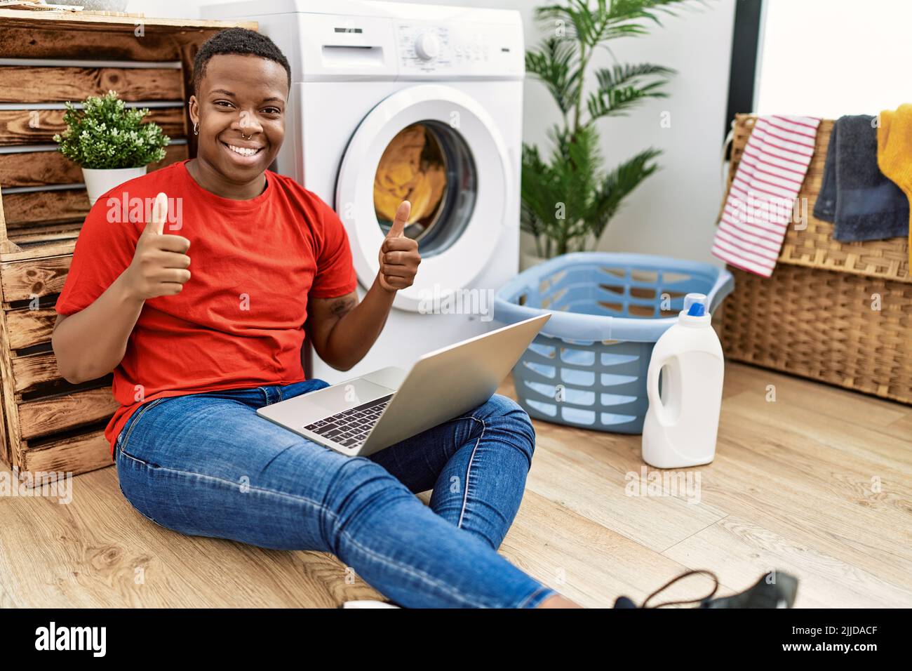 Young african man doing laundry and using computer success sign doing ...