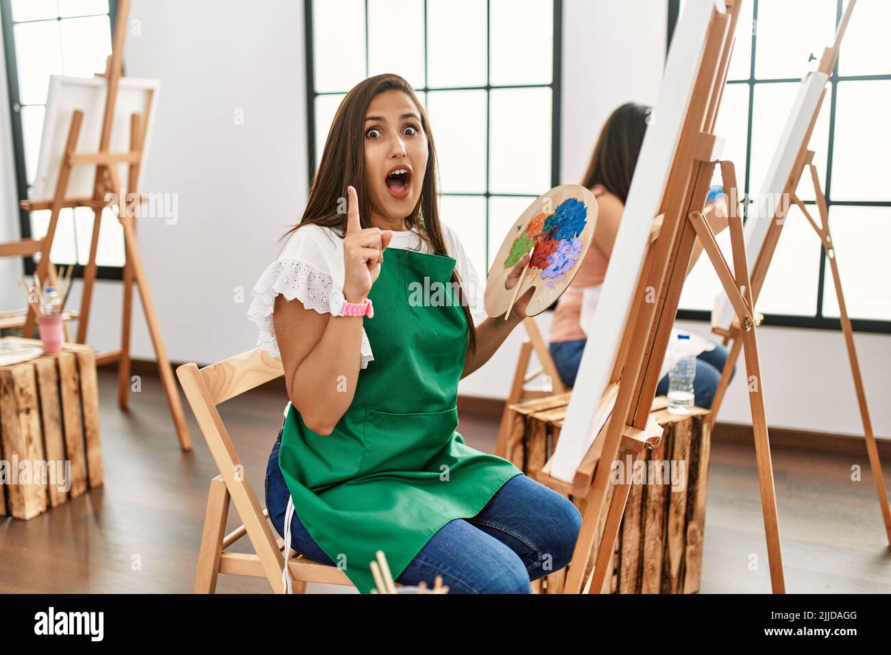 Young hispanic artist women painting on canvas at art studio pointing ...