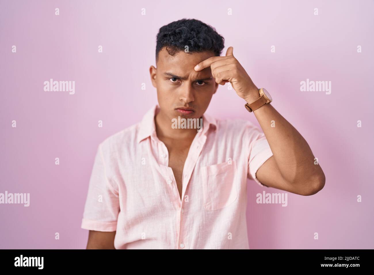 Young hispanic man standing over pink background pointing unhappy to ...