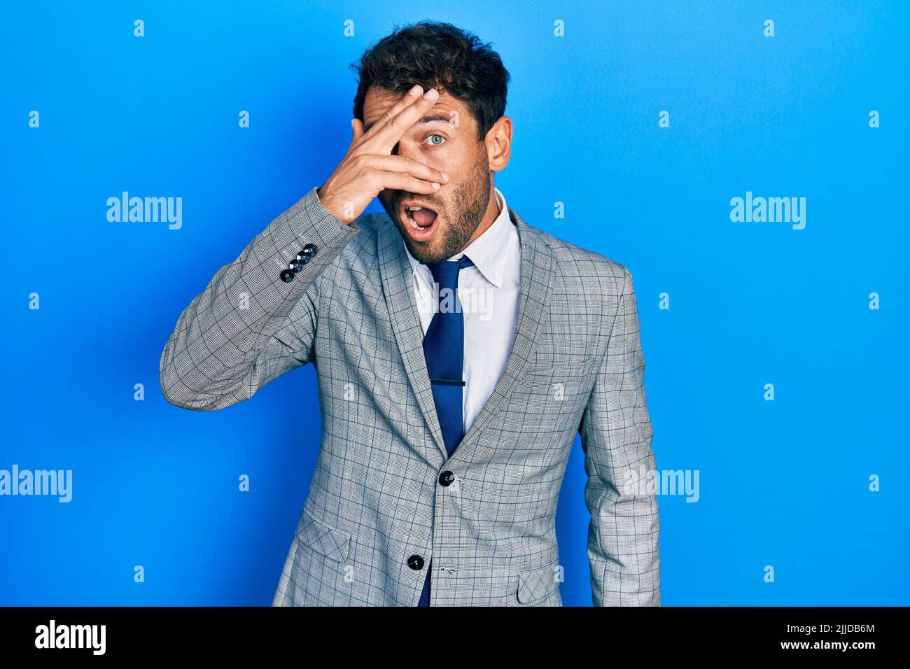 Handsome man with beard wearing business suit and tie peeking in shock ...
