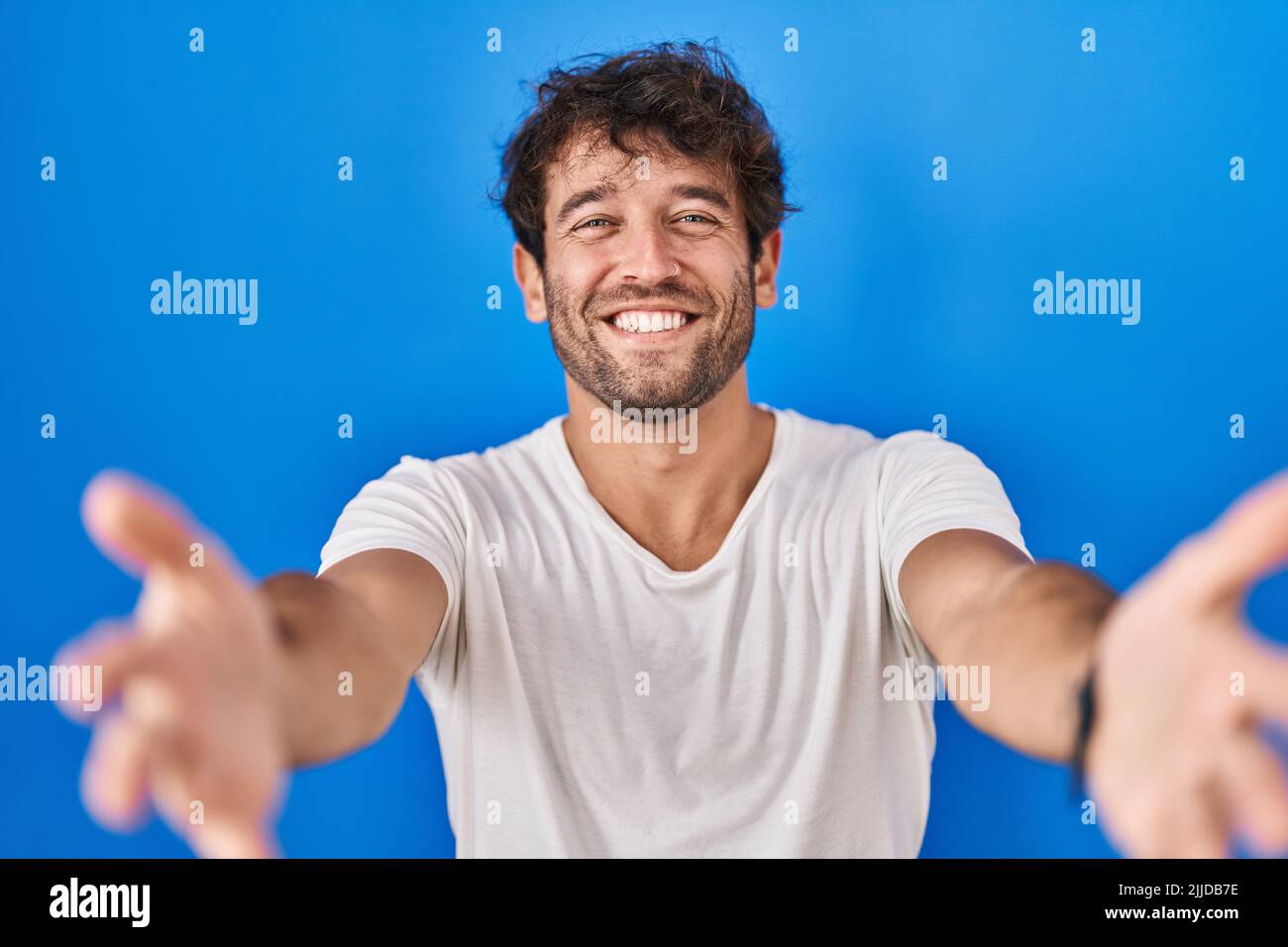 Hispanic young man standing over blue background smiling cheerful ...