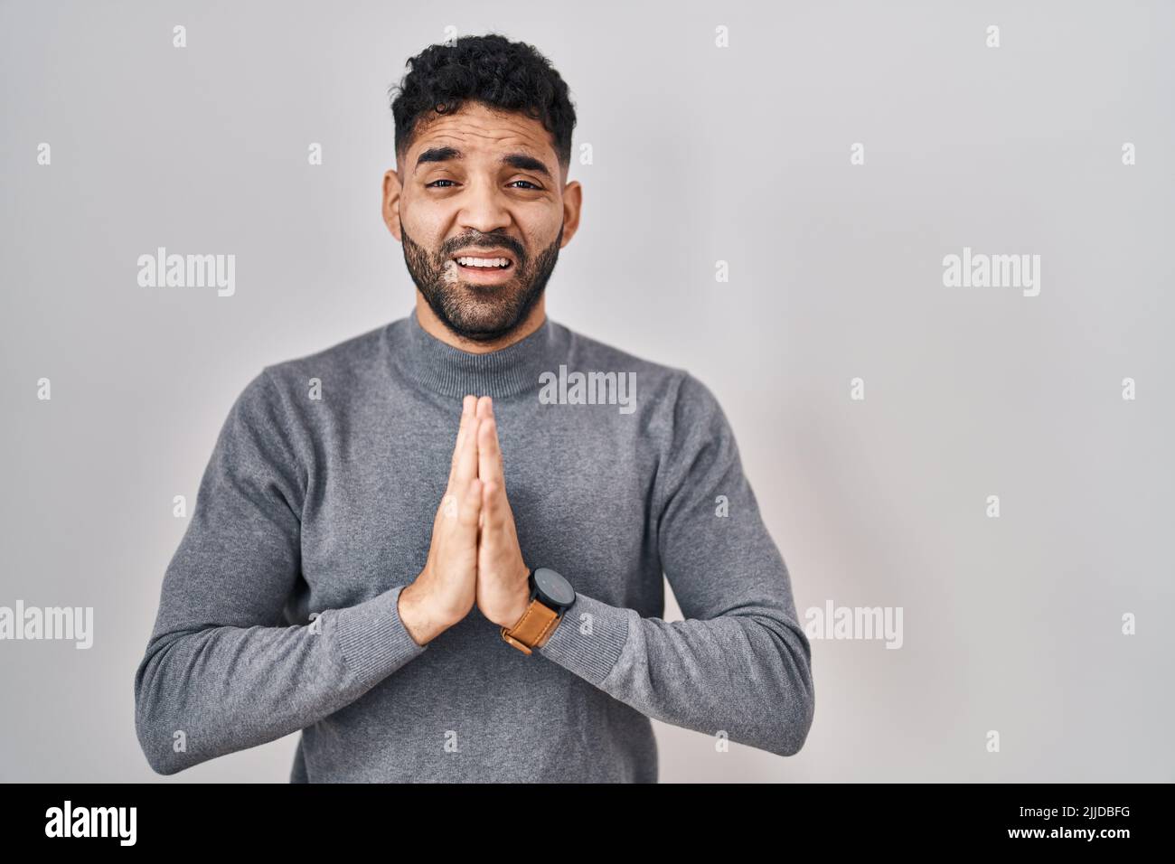 Hispanic man with beard standing over white background begging and ...