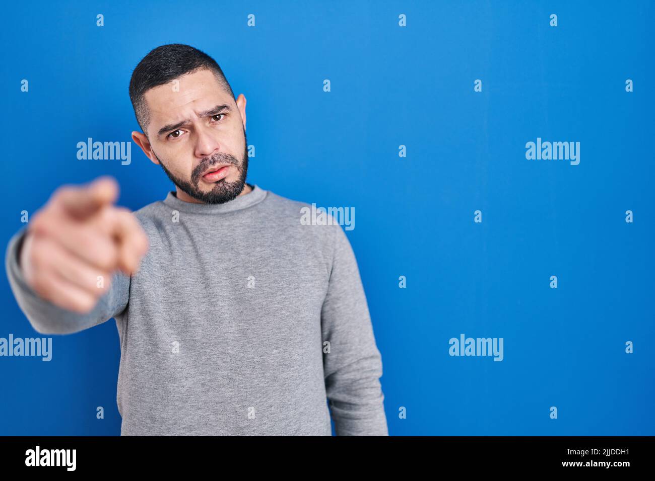 Hispanic man standing over blue background pointing displeased and ...