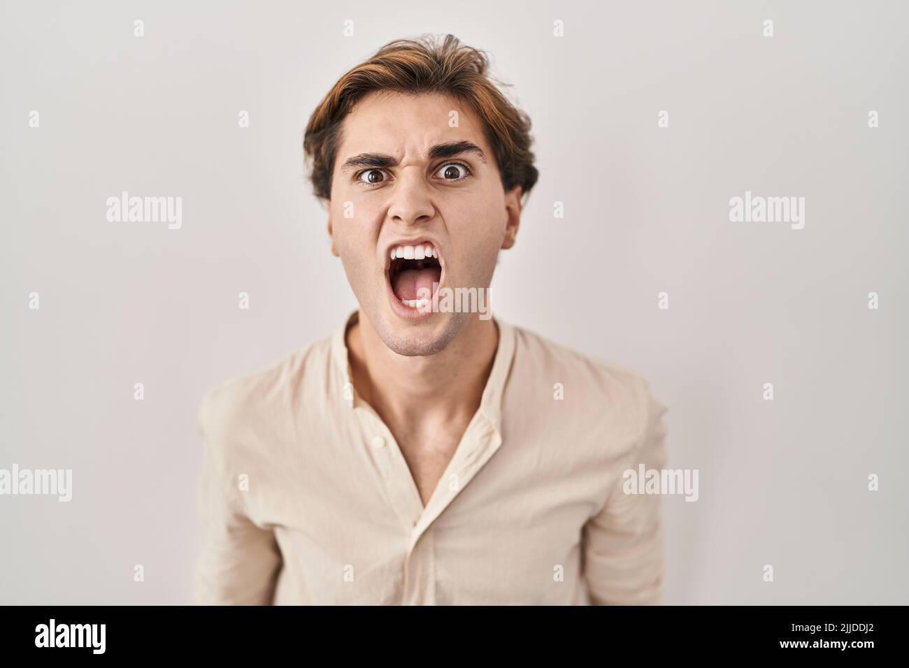 Young man standing over isolated background angry and mad screaming ...