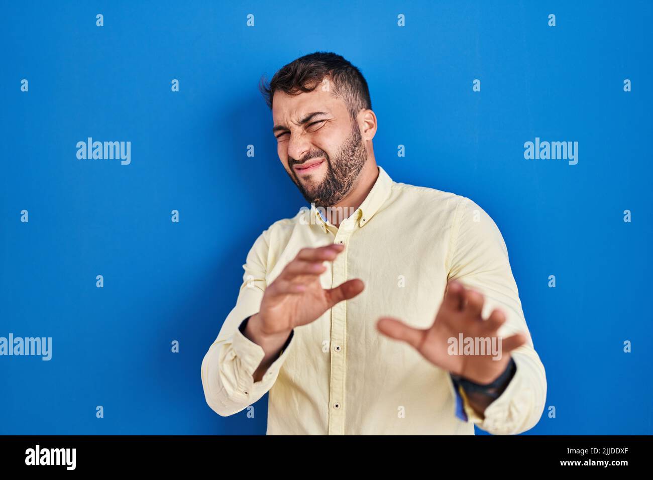 Handsome hispanic man standing over blue background disgusted ...