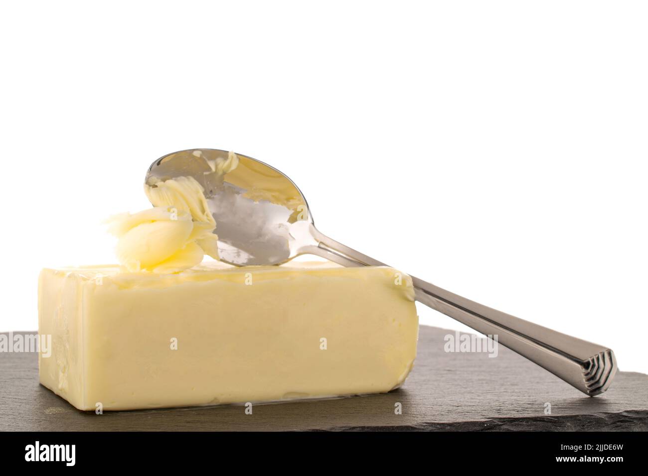 One piece of butter with a metal spoon on a shale stone, close-up ...