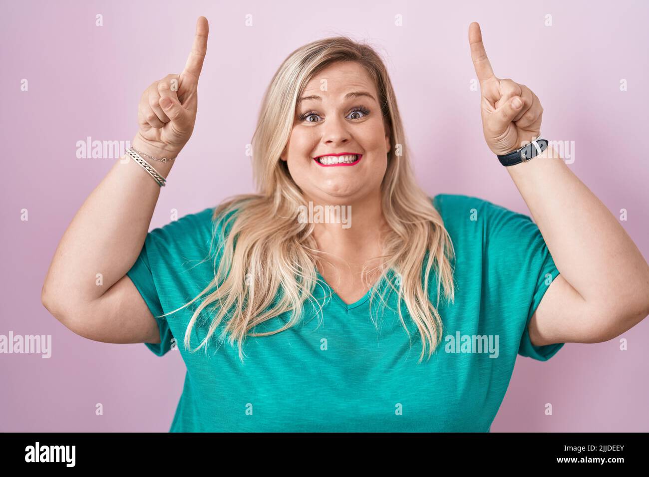 Caucasian plus size woman standing over pink background smiling amazed ...