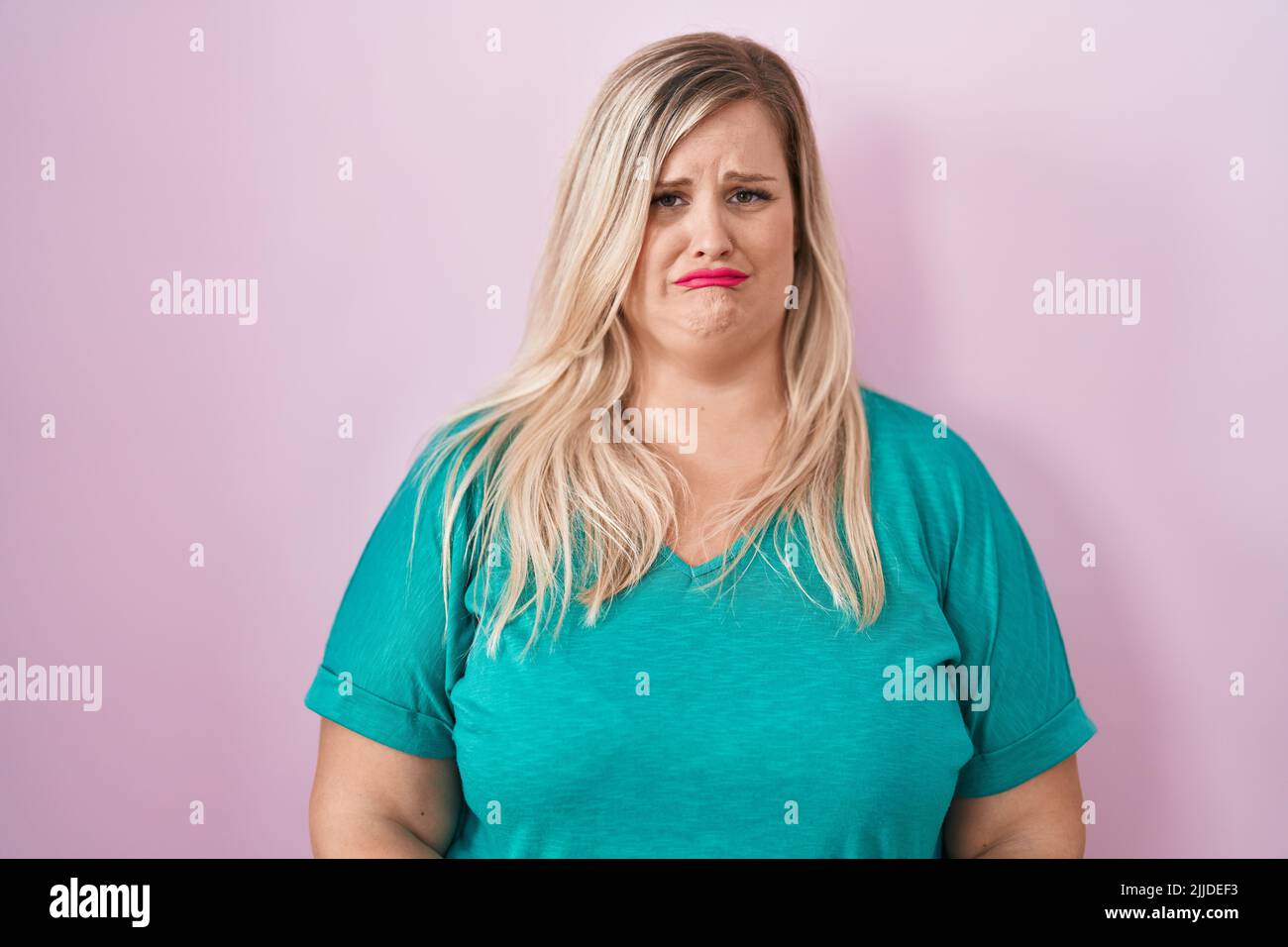 Caucasian plus size woman standing over pink background depressed and ...