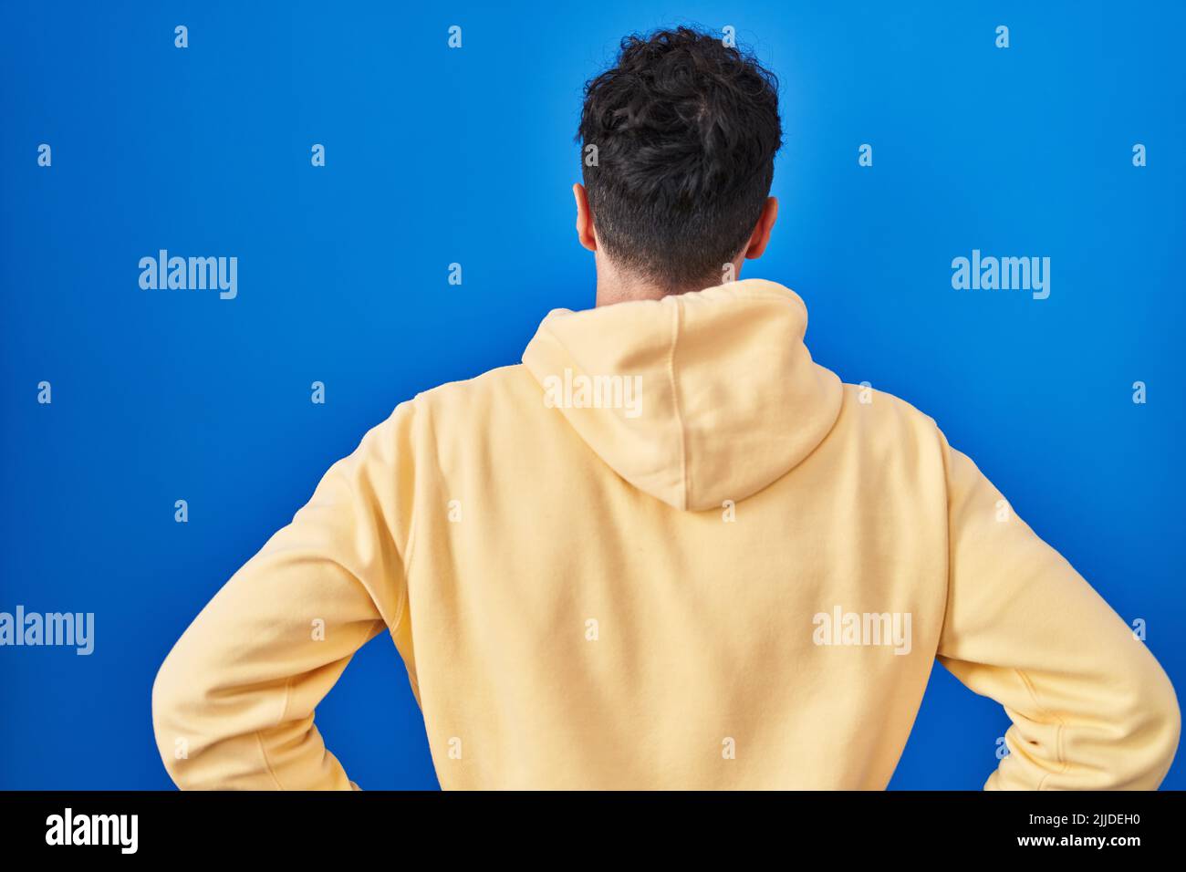 Hispanic man standing over blue background standing backwards looking ...