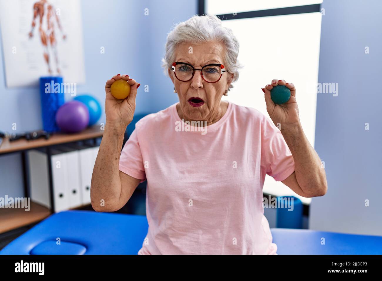 Senior woman with grey hair holding hands strength balls in shock face ...