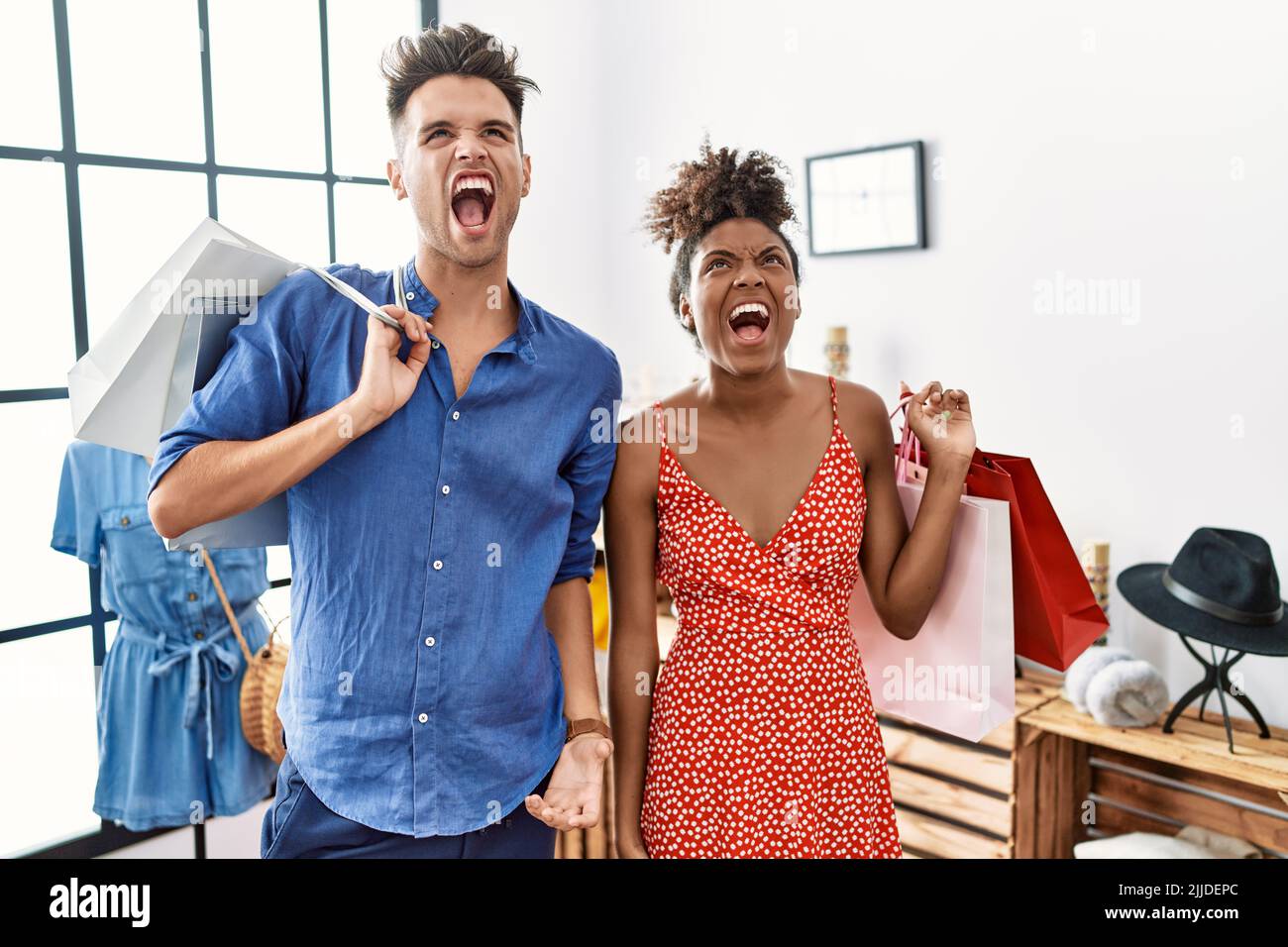 Young interracial couple holding shopping bags at retail shop angry and ...