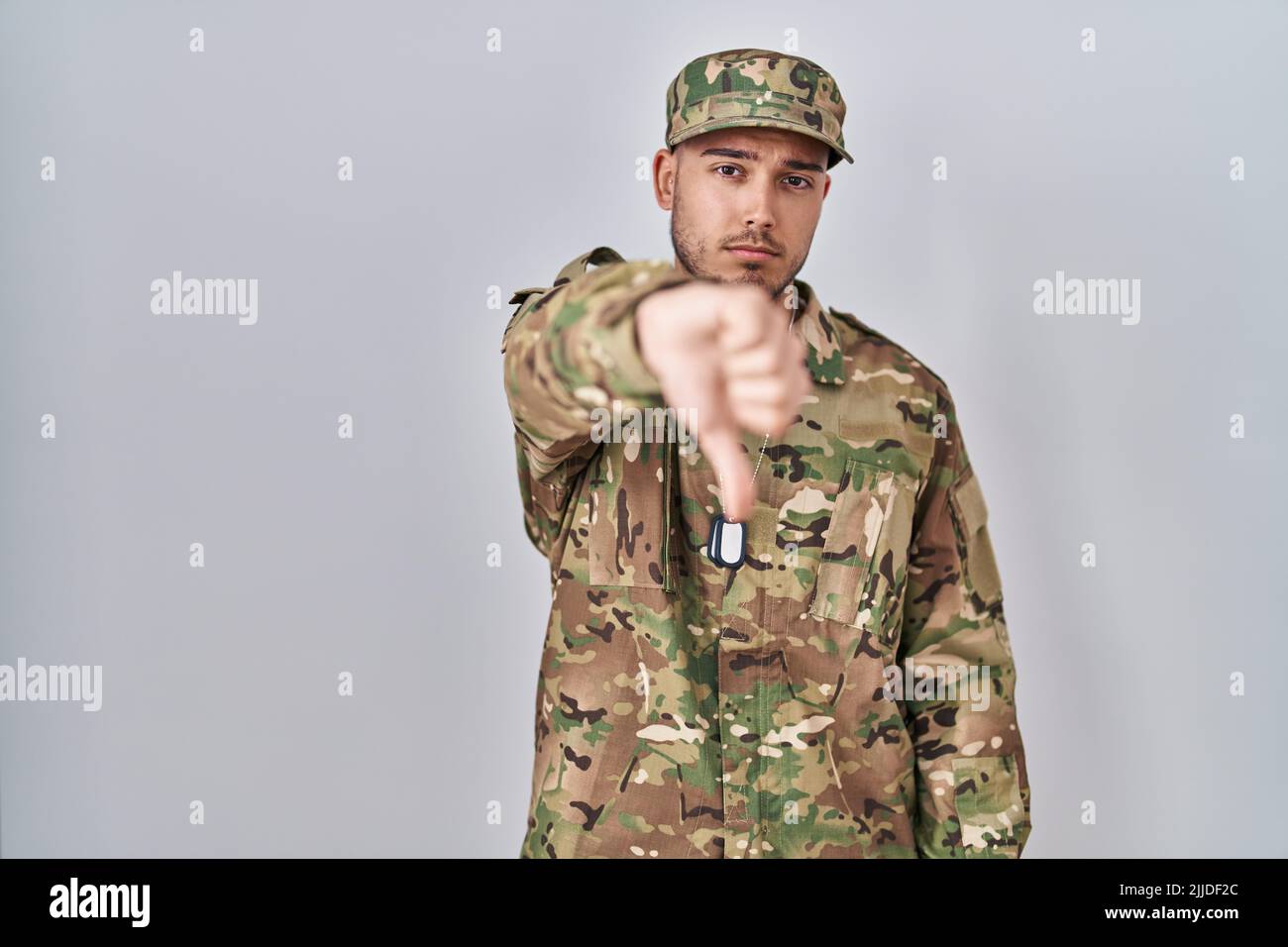 Young hispanic man wearing camouflage army uniform looking unhappy and ...
