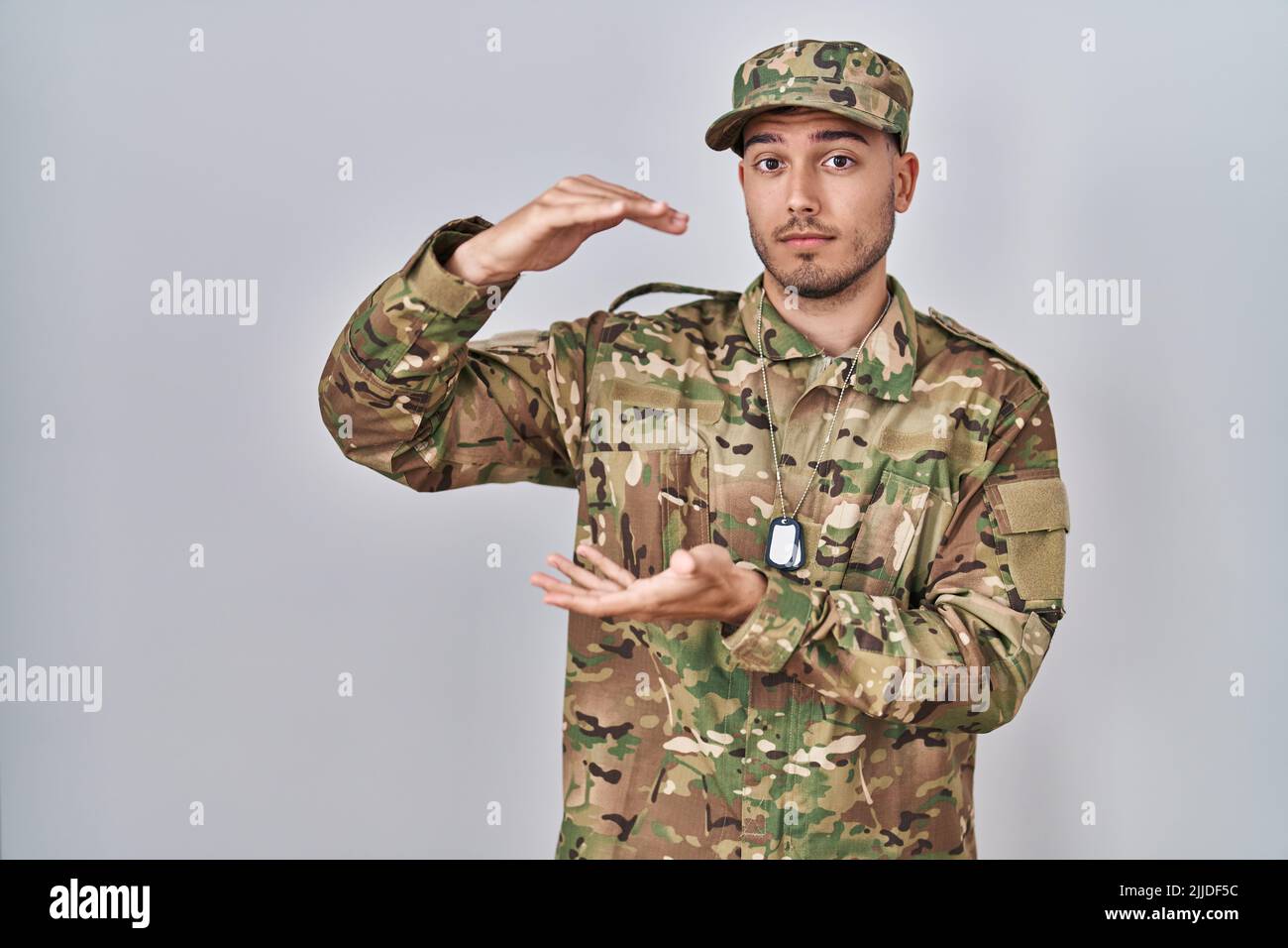 Young hispanic man wearing camouflage army uniform gesturing with hands ...