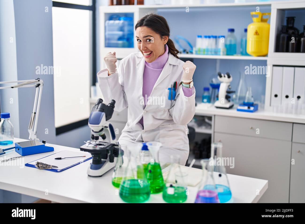 Young brunette woman working at scientist laboratory screaming proud ...