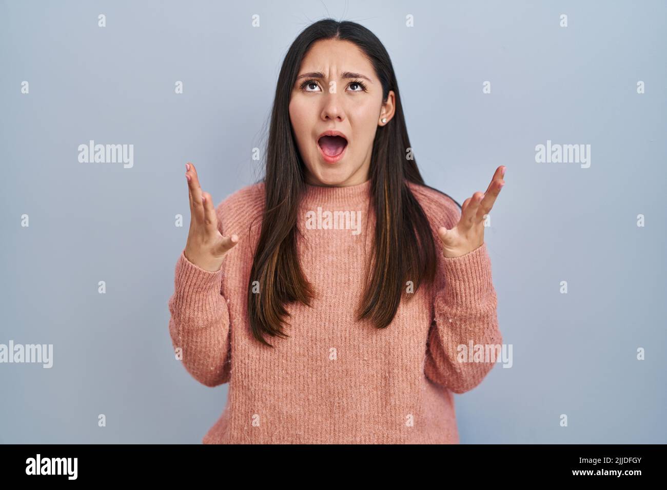 Young latin woman standing over blue background crazy and mad shouting ...