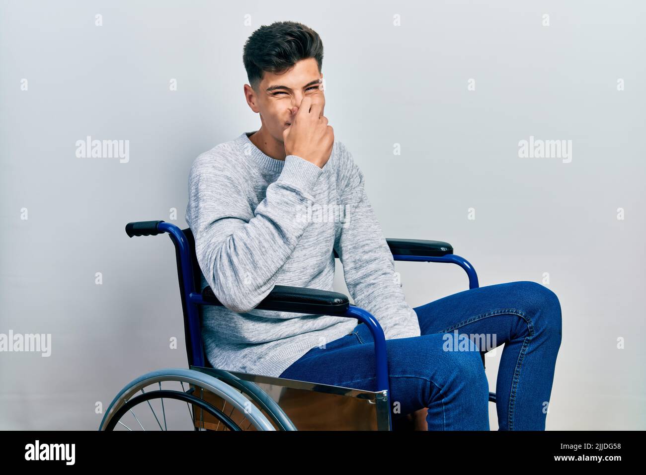 Young hispanic man sitting on wheelchair smelling something stinky and ...