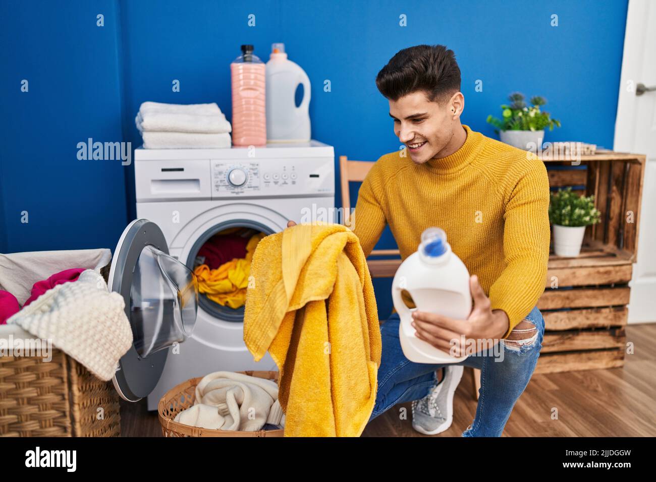 Young hispanic man washing clothes holding detergent bottle at laundry ...