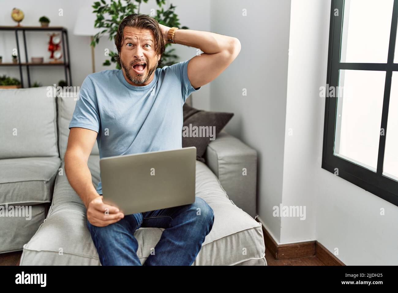 Handsome middle age man using computer laptop on the sofa crazy and ...