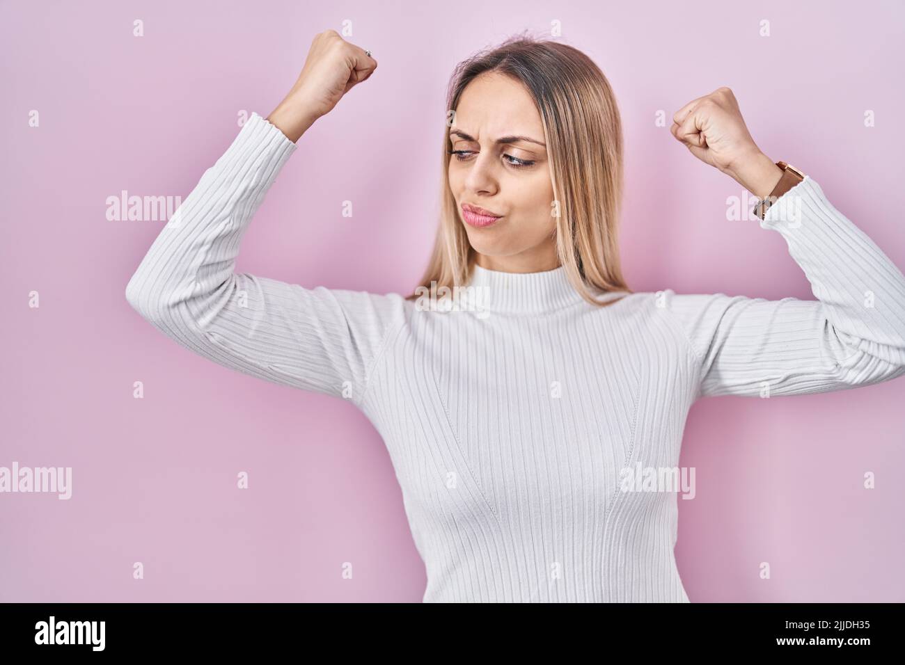 Young blonde woman wearing white sweater over pink background showing ...