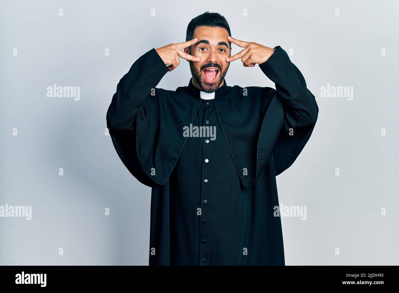 Handsome hispanic man with beard wearing catholic priest robe doing ...